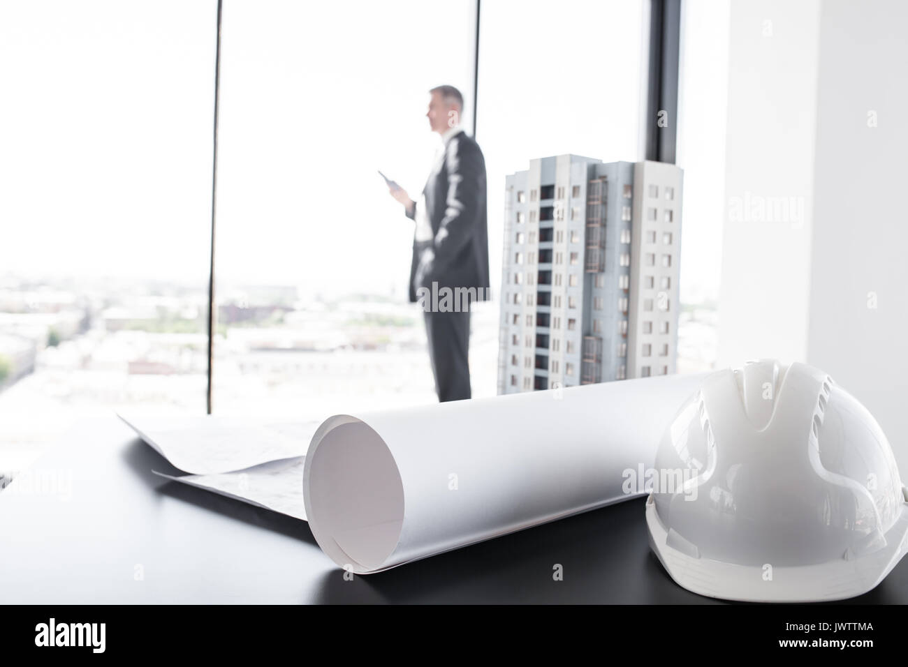 Businessman in construction company office, model of modern multi ...