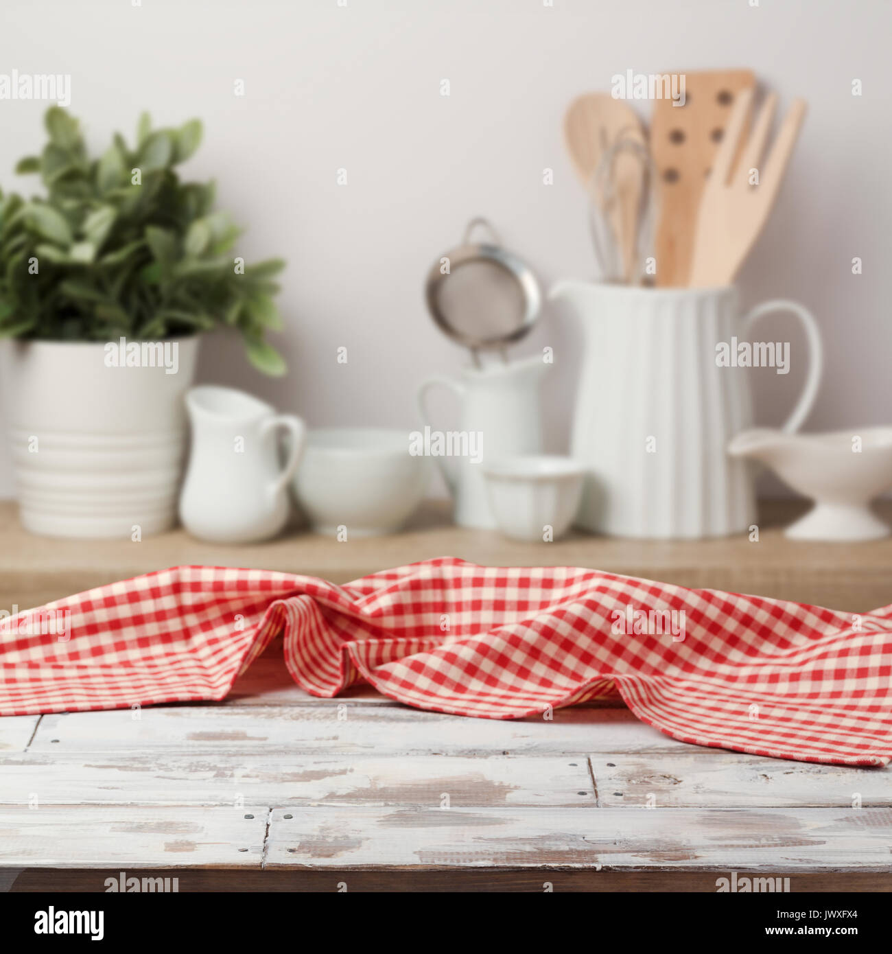 Empty wooden table with red checked tablecloth over kitchen shelf ...