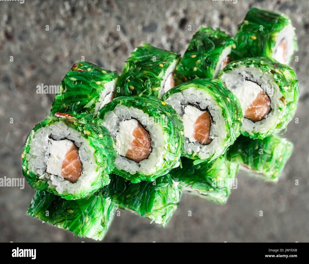 Green roll made with salmon, chuka and cream cheese over concrete ...