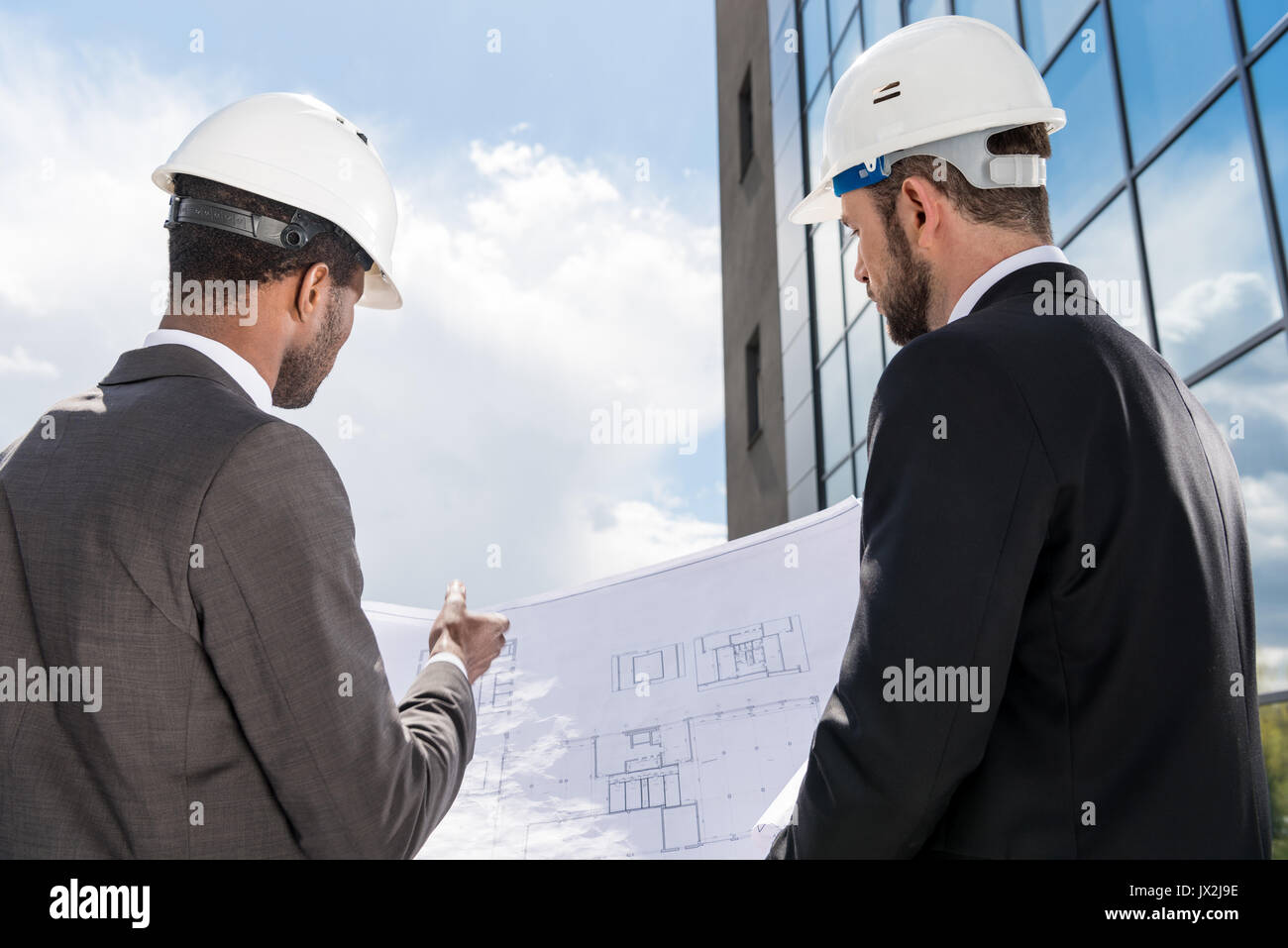 Back view of professional architects in hardhats working with blueprint ...