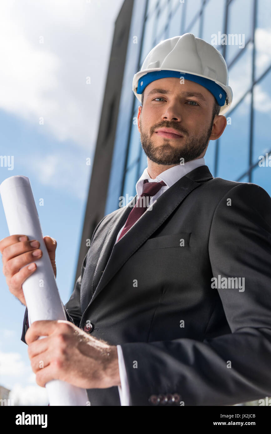 Professional architect in hard hat holding blueprint and looking at ... Professional architect in hard hat holding blueprint and looking at ...