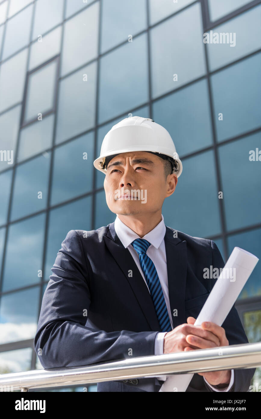 portrait of pensive professional architect in hard hat holding ...