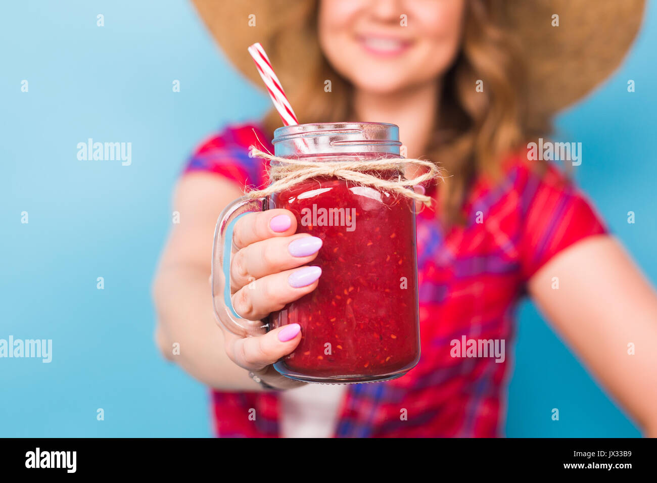 smiling woman drink red juice. studio portrait with blue background and ...
