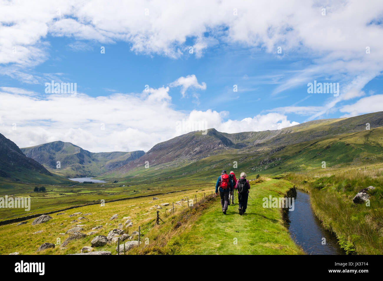 Hikers hiking along a leat watercourse with view along Ogwen valley in ...