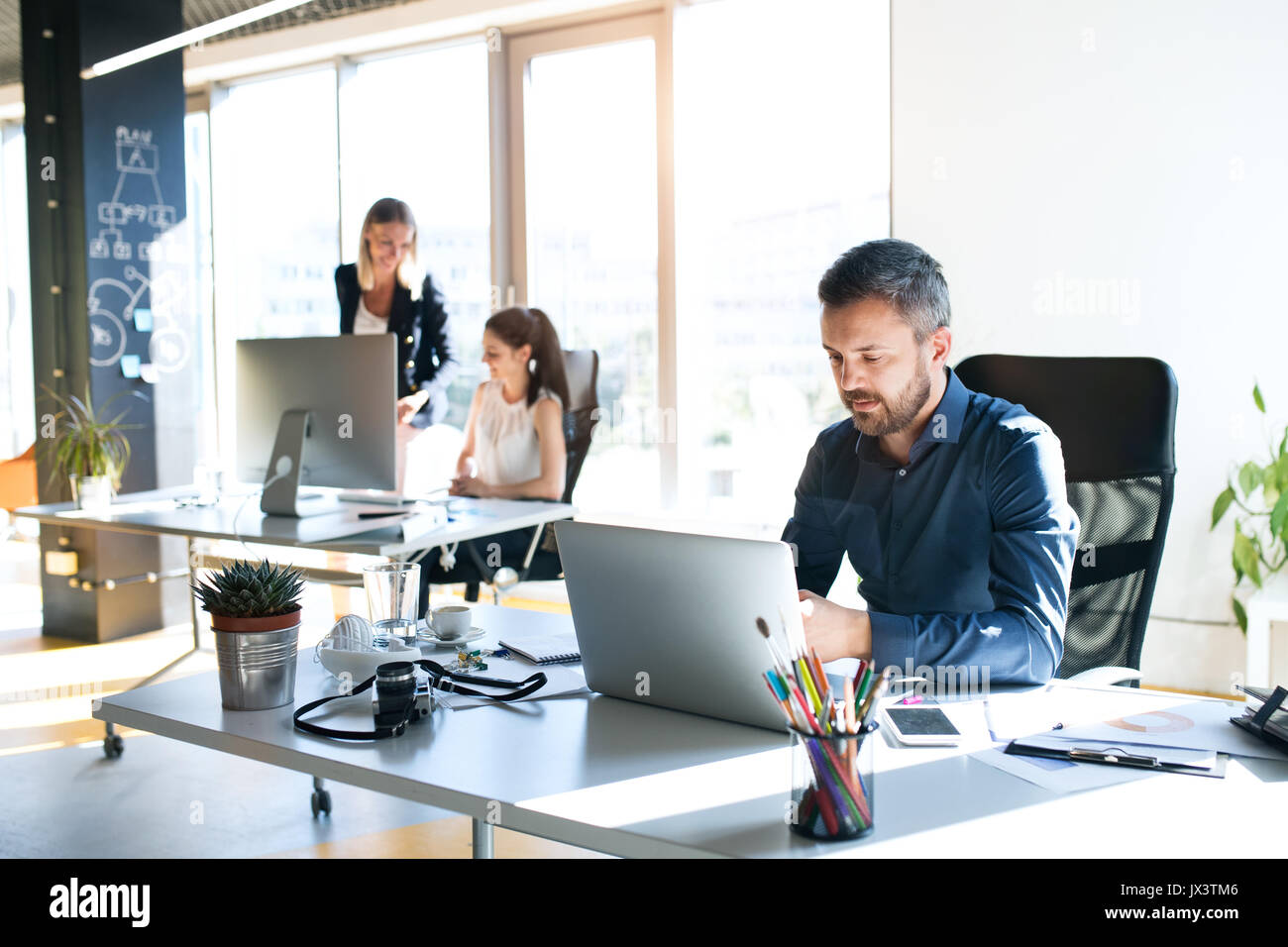 Three business people in the workplace. Two women and man sitting in ...