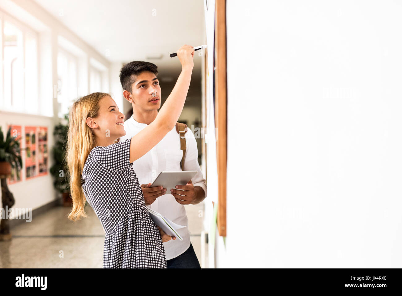 Attractive teenage student couple in high school hall writing something ...