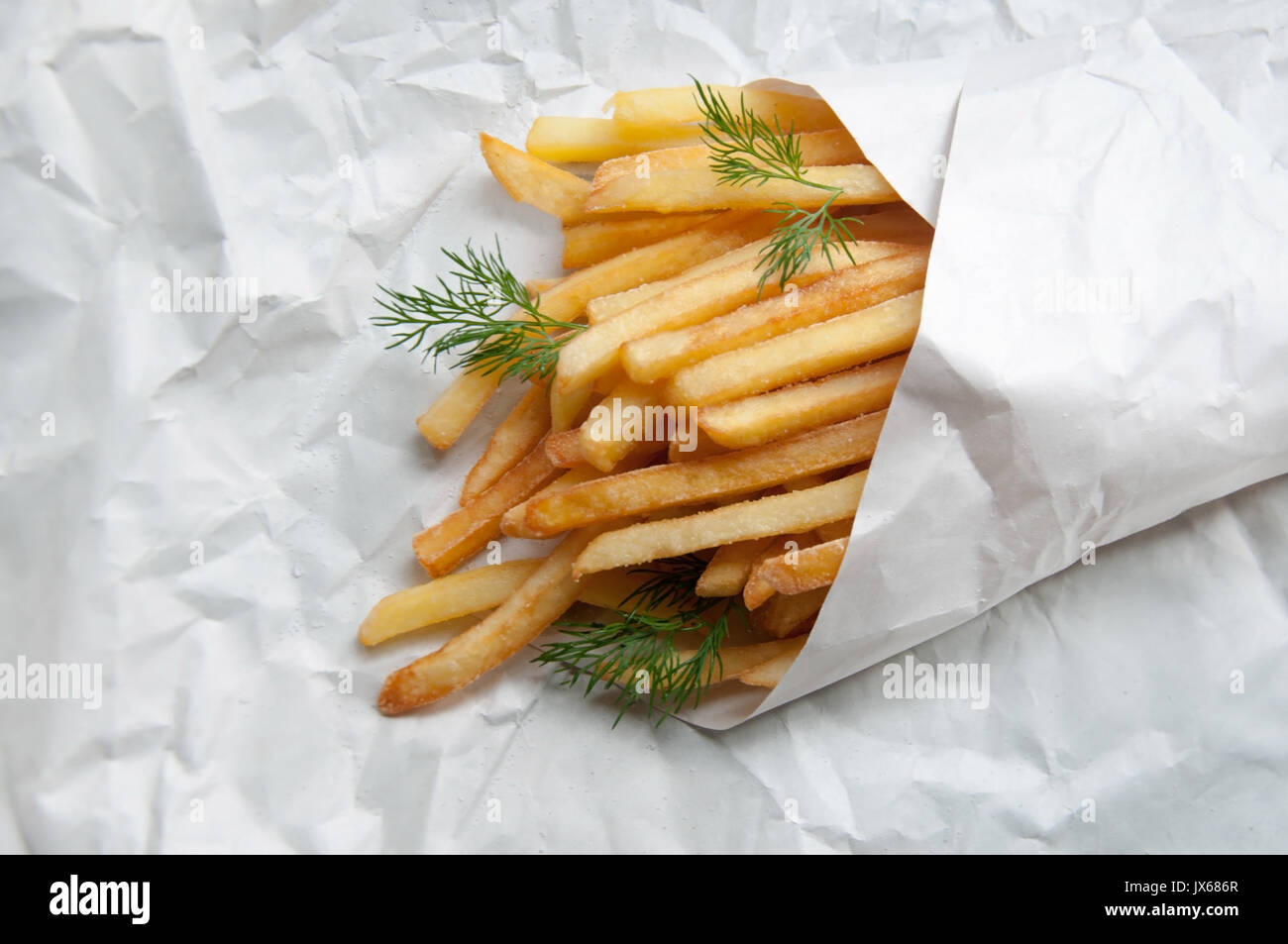 Potatoes French fries in a white paper bag on a sheet of light paper ...