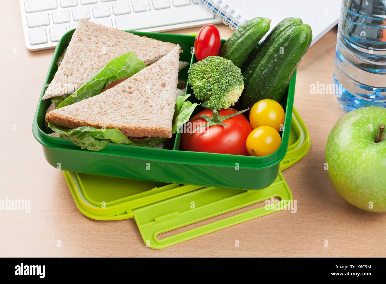 Office desk with supplies and lunch box with vegetables and sandwich ...