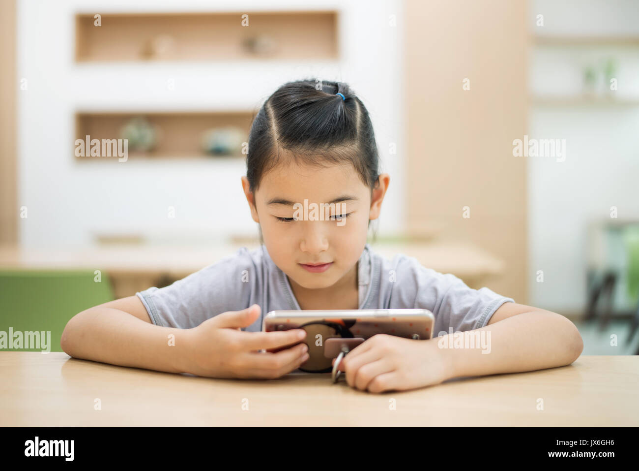 Asian child looking at smartphone at library desk Stock Photo - Alamy