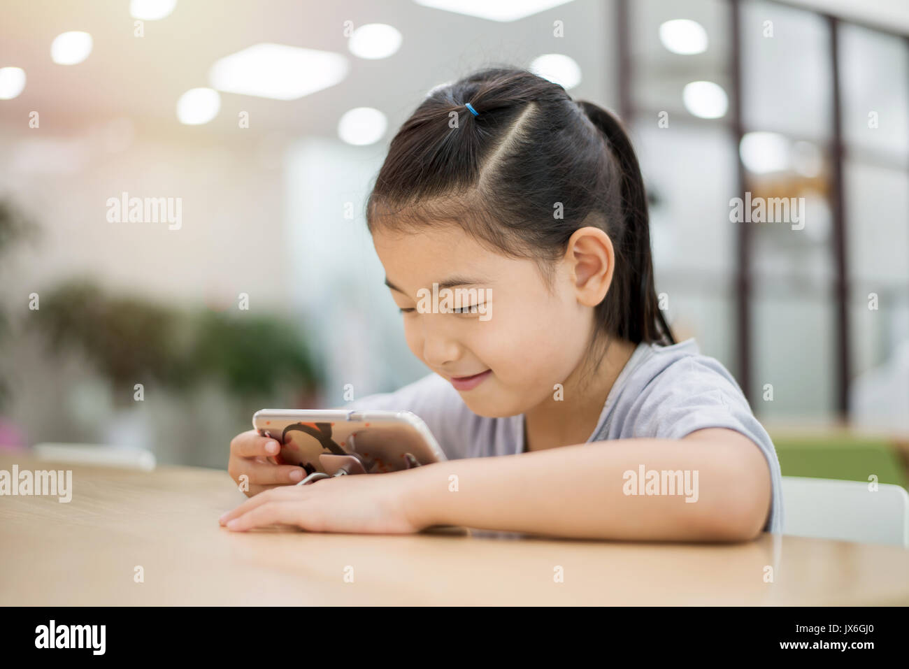 Asian child looking at smartphone at library desk Stock Photo - Alamy