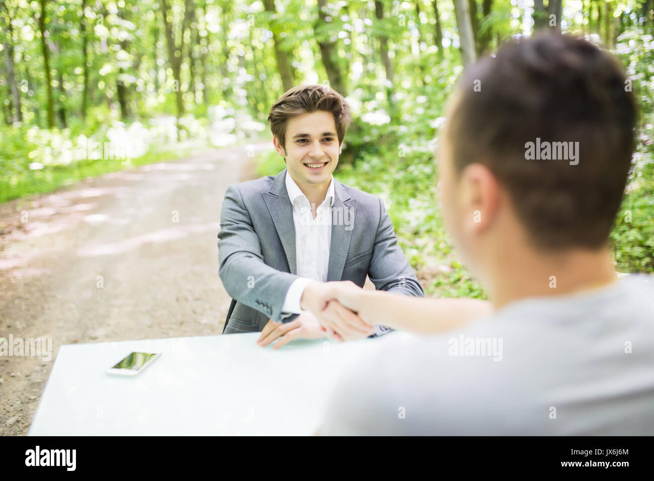 Business man in suit handshake with client at his office table in green ...
