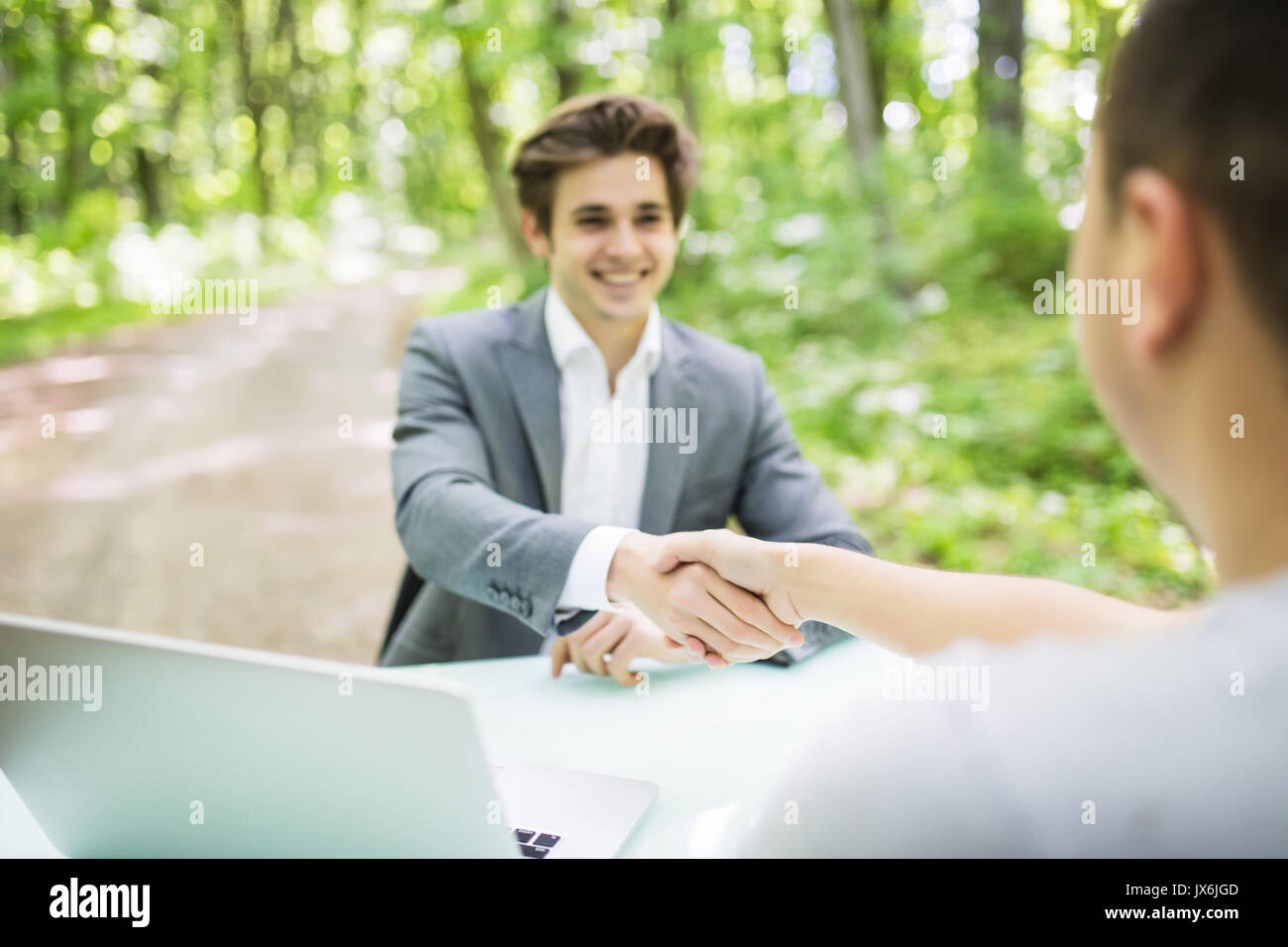 Business man in suit handshake with client at his office table in green ...