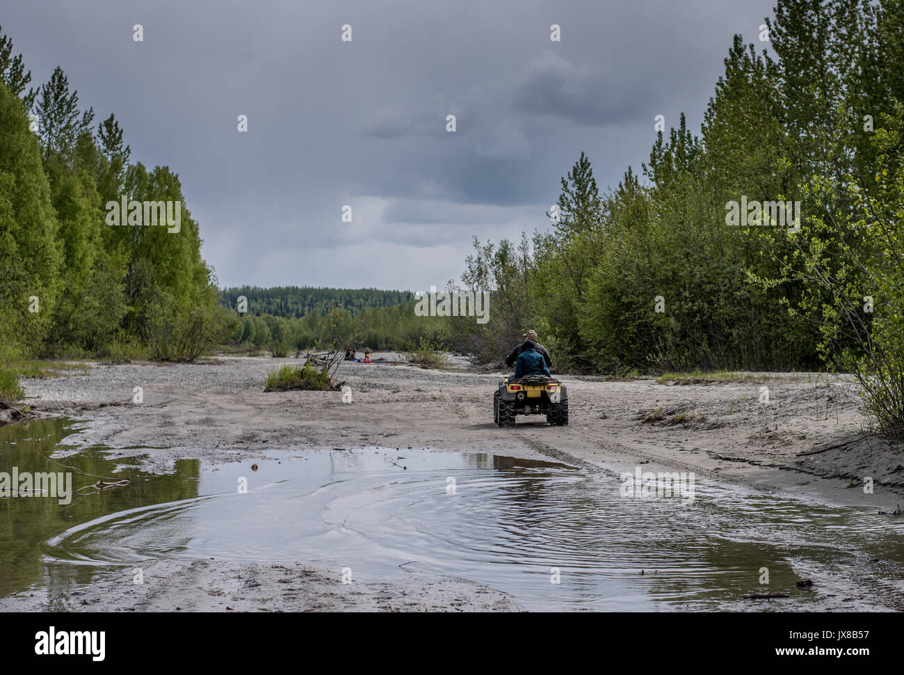 Dad and son riding their ATV through water and sand Stock Photo - Alamy