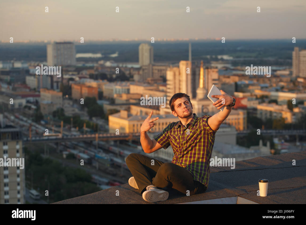 A hipster guy makes a selfie on the roof of a high-rise building. The ...