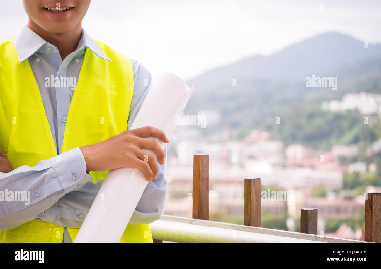 A construction engineer. Wearing a helmet and vest holding a roll of ...