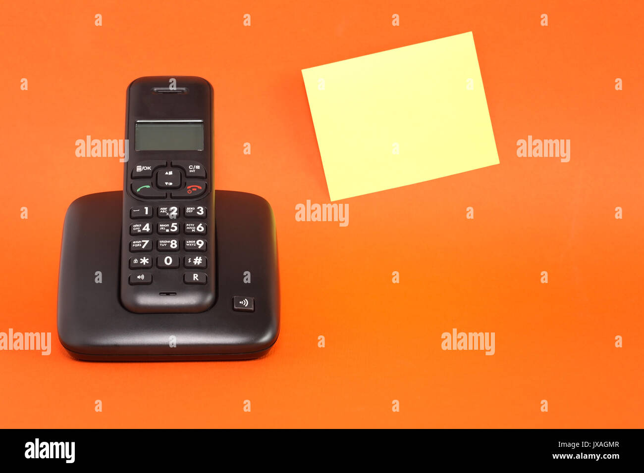 Modern black wireless telephone near blank yellow adhesive note on red ...