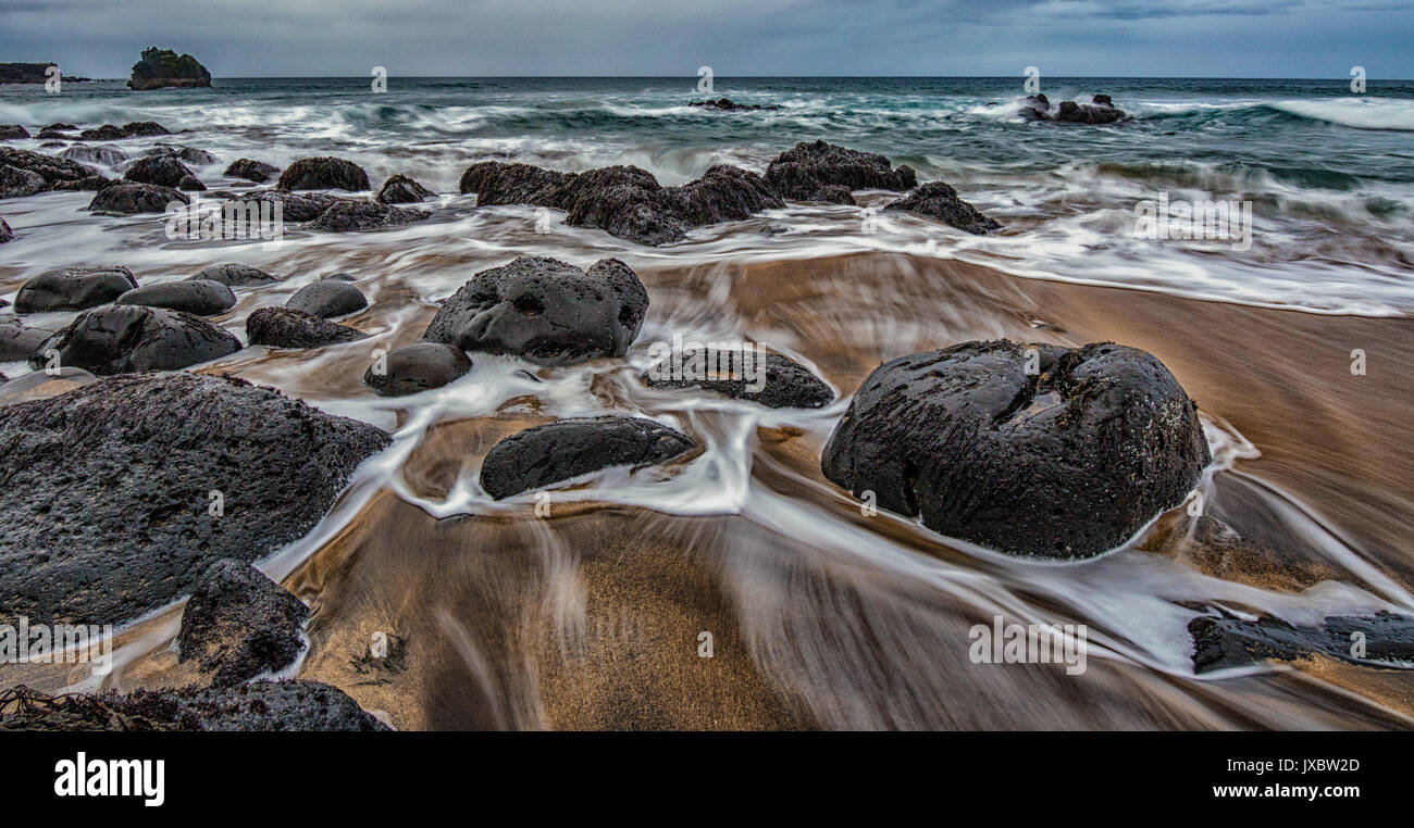The tide comes in over rocks and sand on the beach at Strondin, Iceland ...