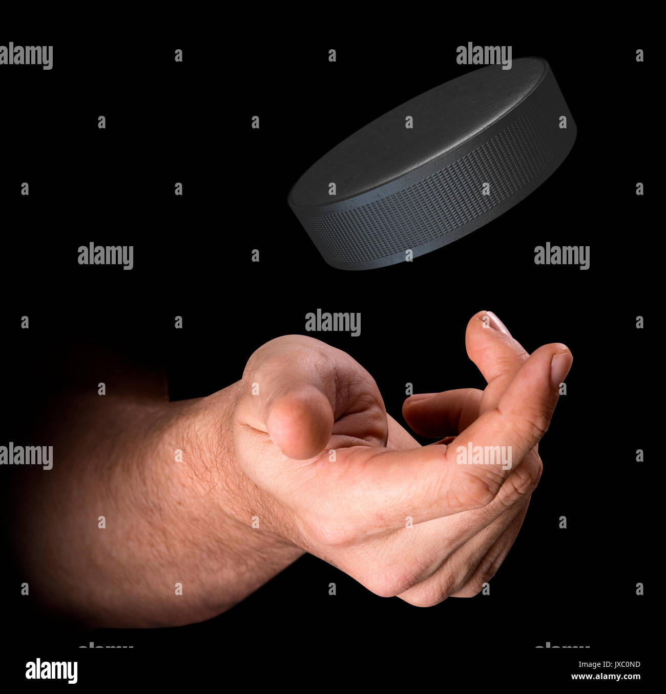 A male hand tossing a hockey puck up in the air on an isolated dark ...
