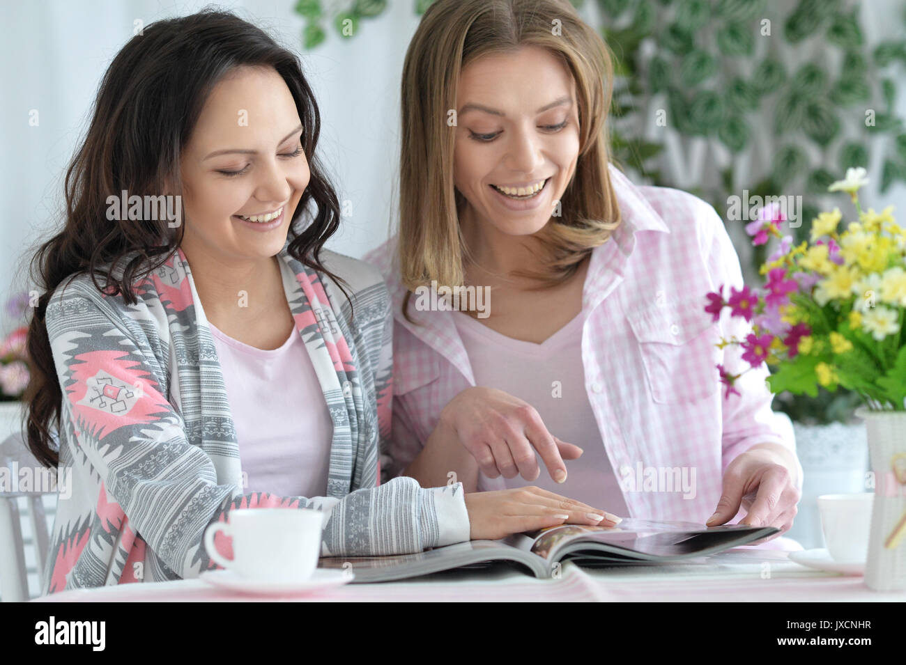 Two female friends reading magazine Stock Photo - Alamy