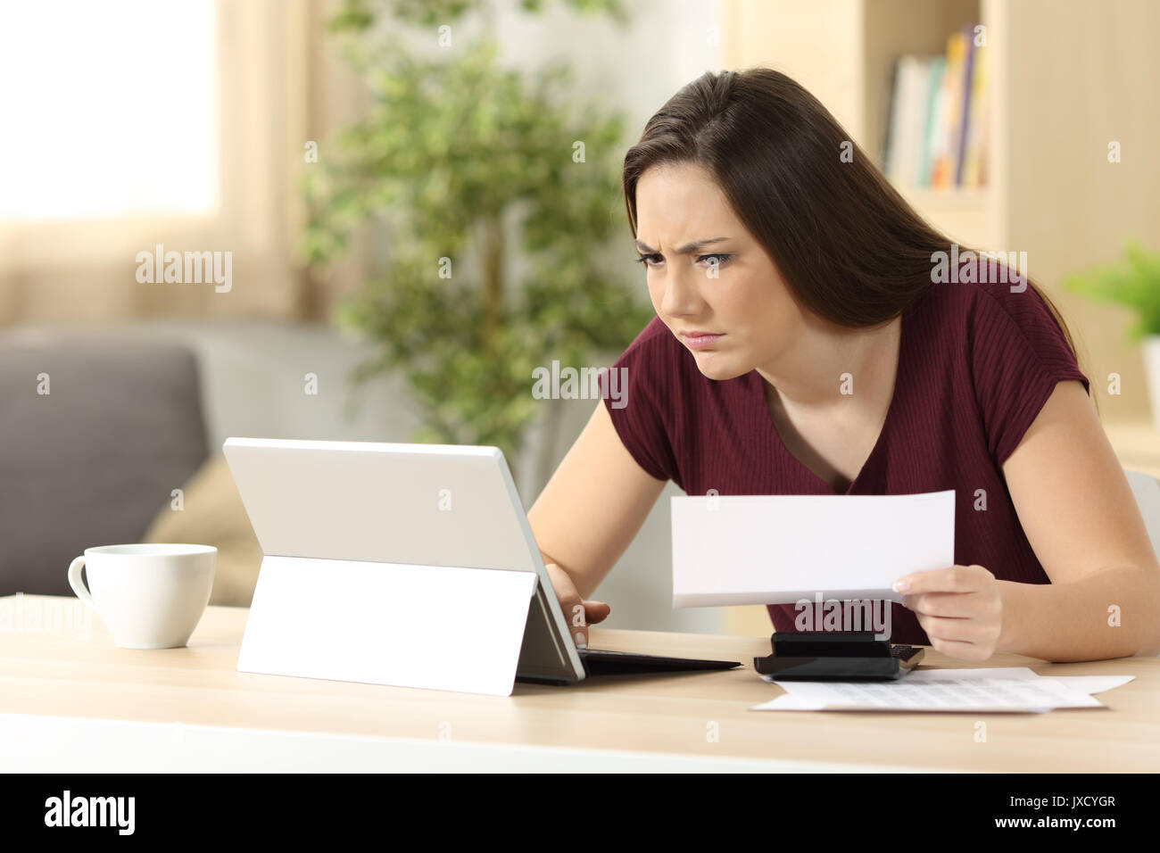 Confused woman comparing on line information sitting in a desk at home ...