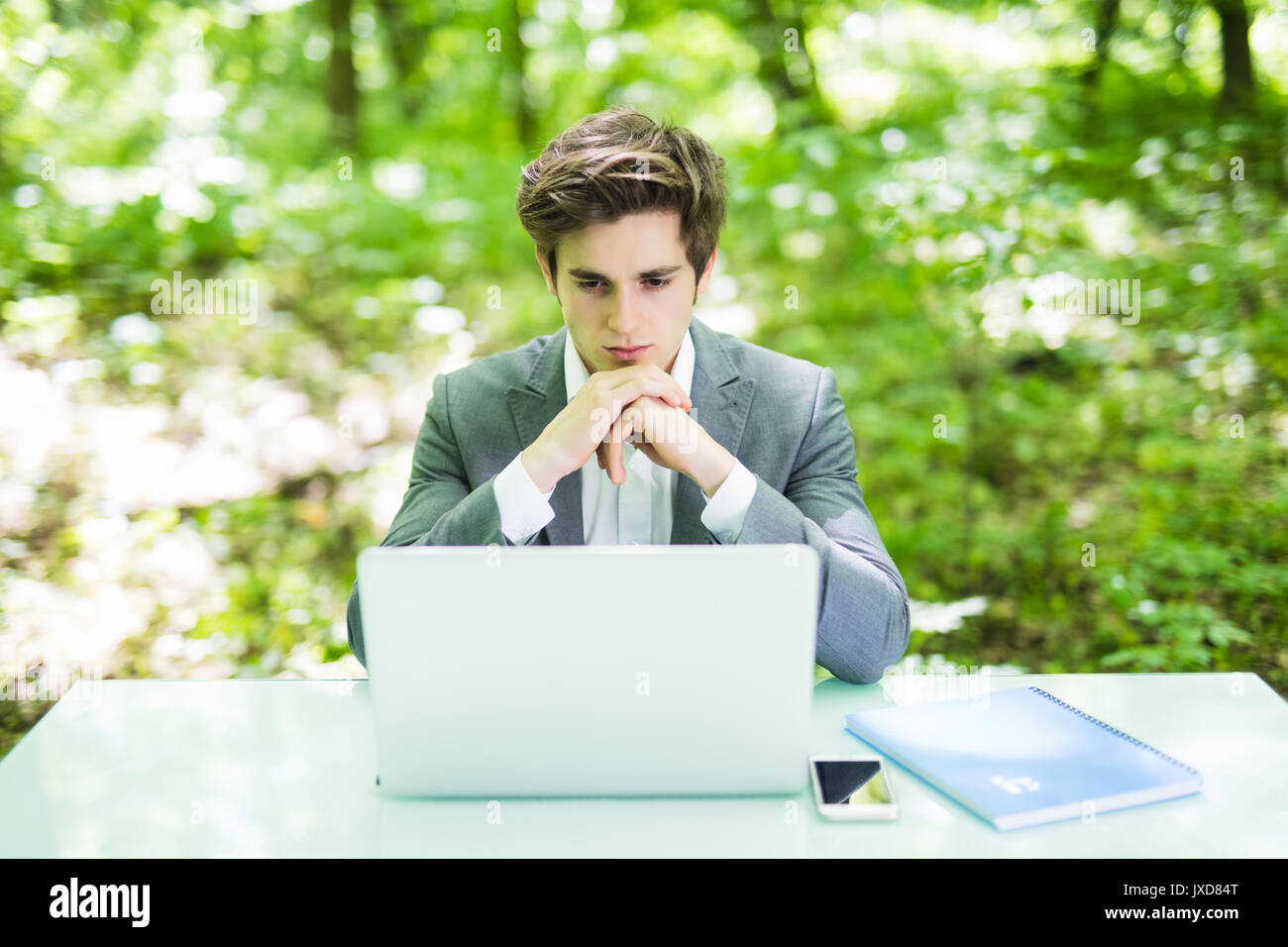Young business man thinking over laptop at office table in green park ...