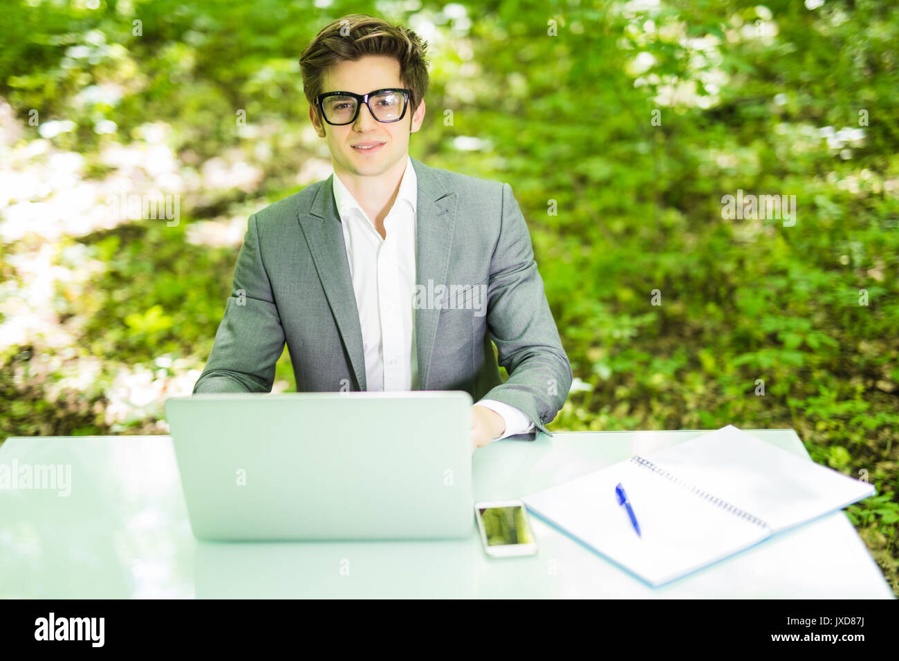 Young freelance working at laptop at office table in green park ...