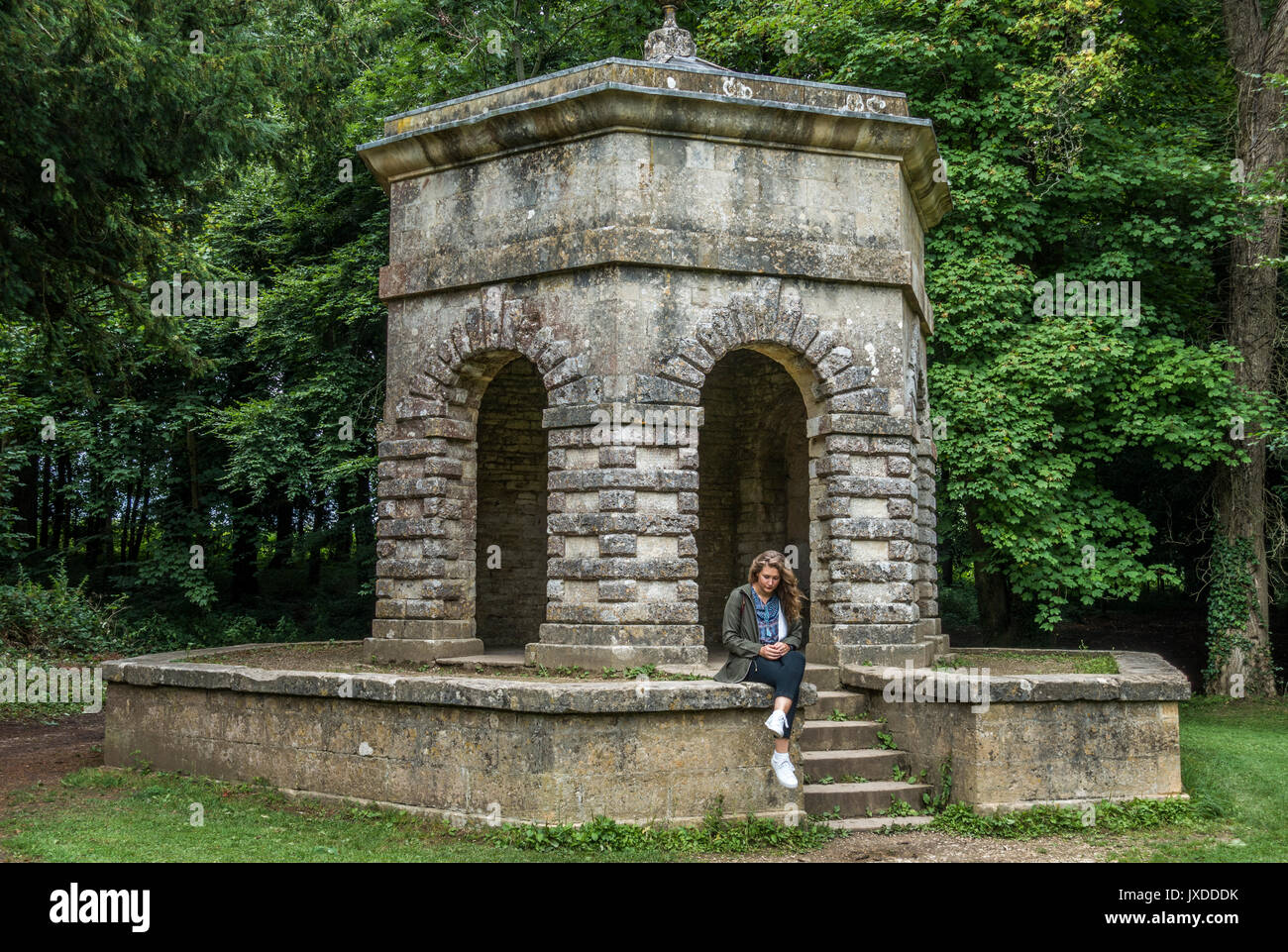 Pretty young woman sitting on The Hexagon Folly in Cirencester Park ...