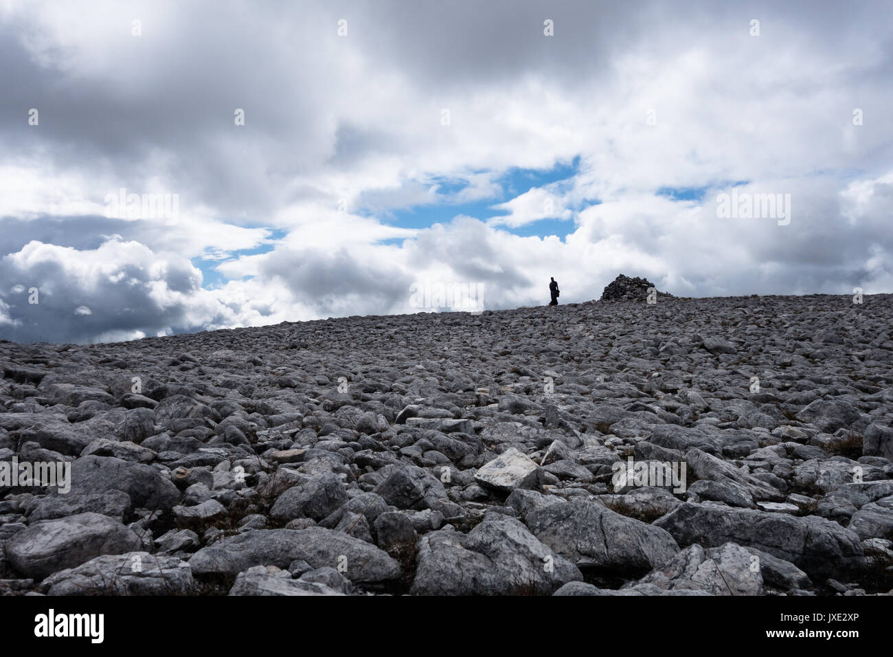 Mountain walker in silhouette against cloudy sky on rock field leading ...