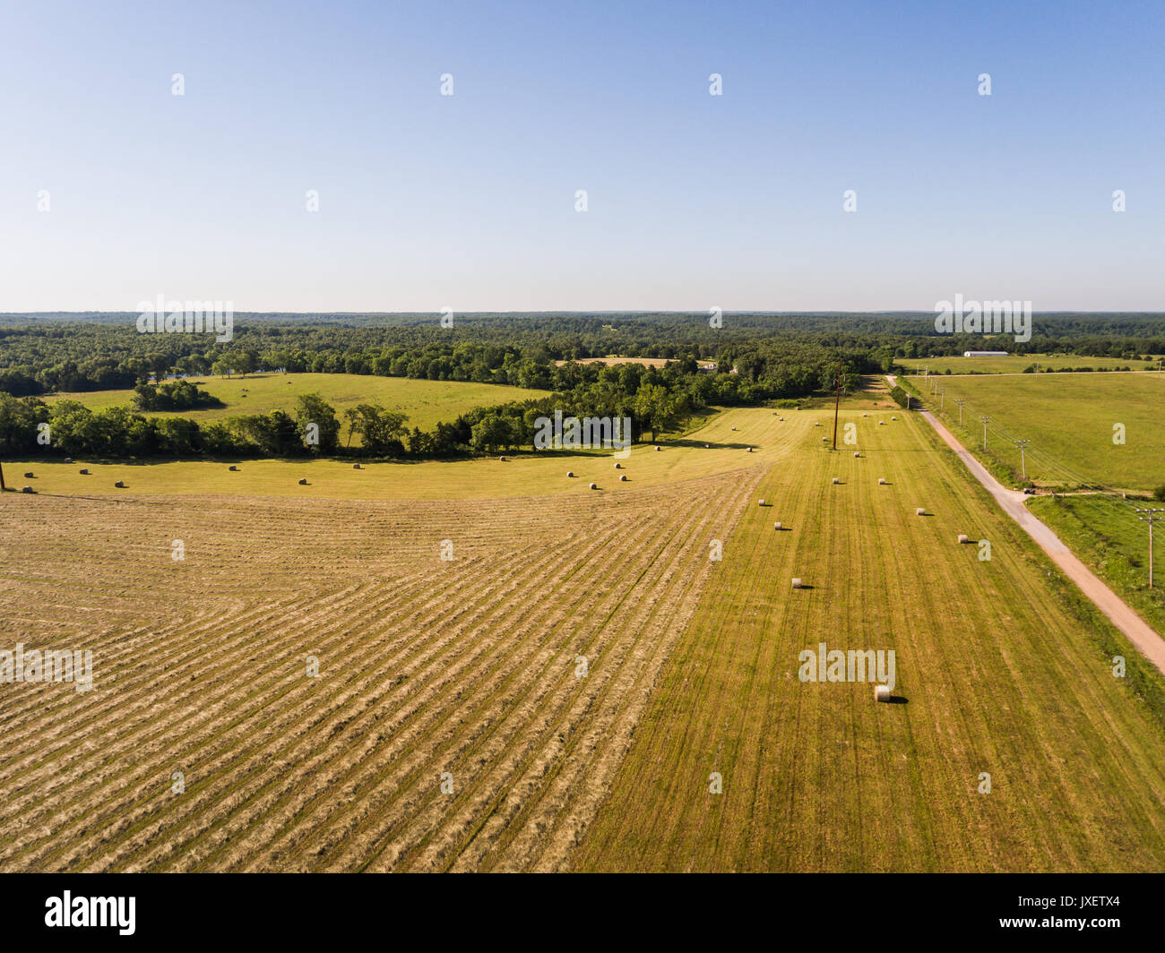 Aerial view of a large field with cut hay and baled hay next to a road ...