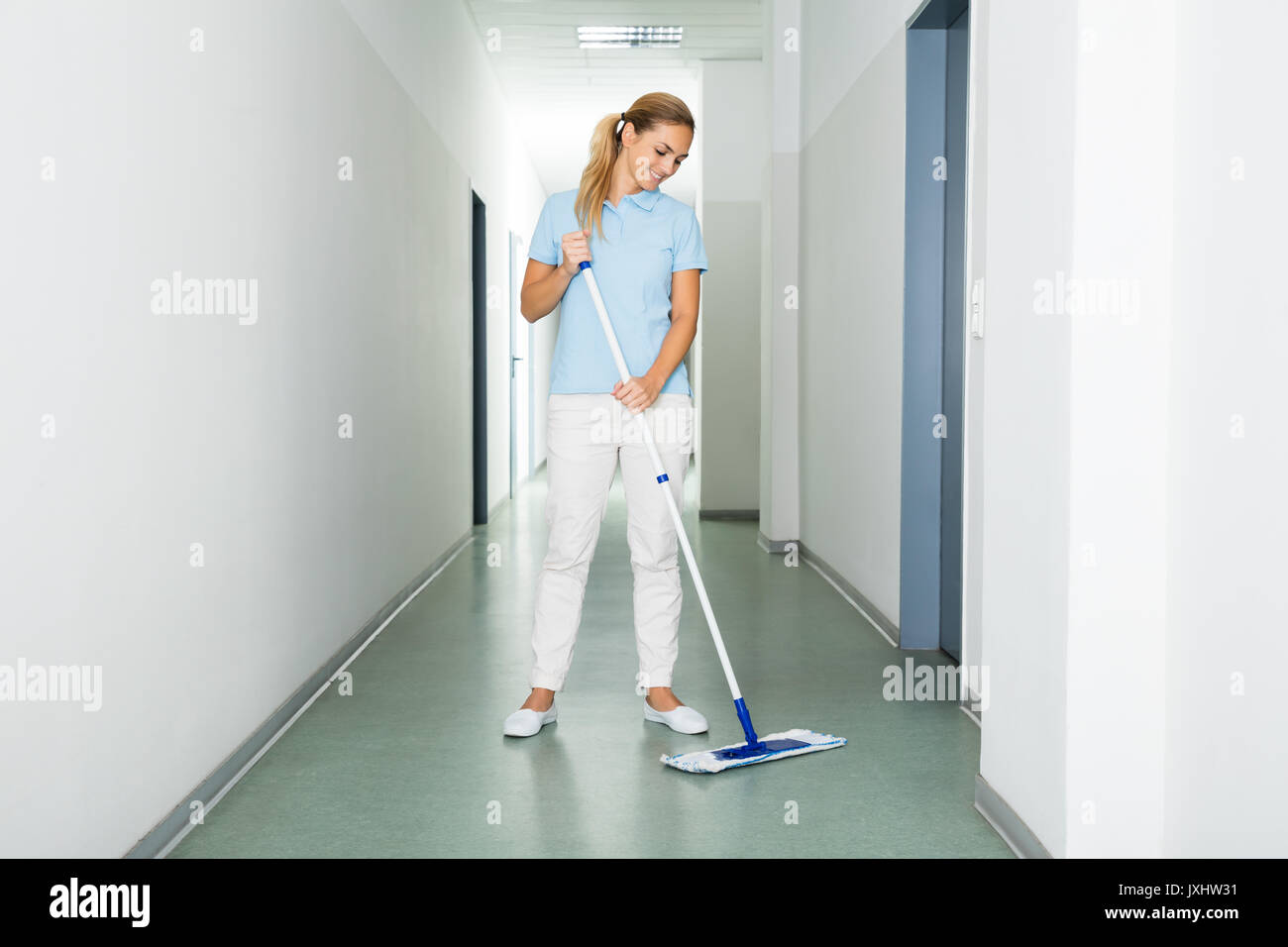 Happy Female Janitor Cleaning The Floor With Mop On The Corridor Of The ...