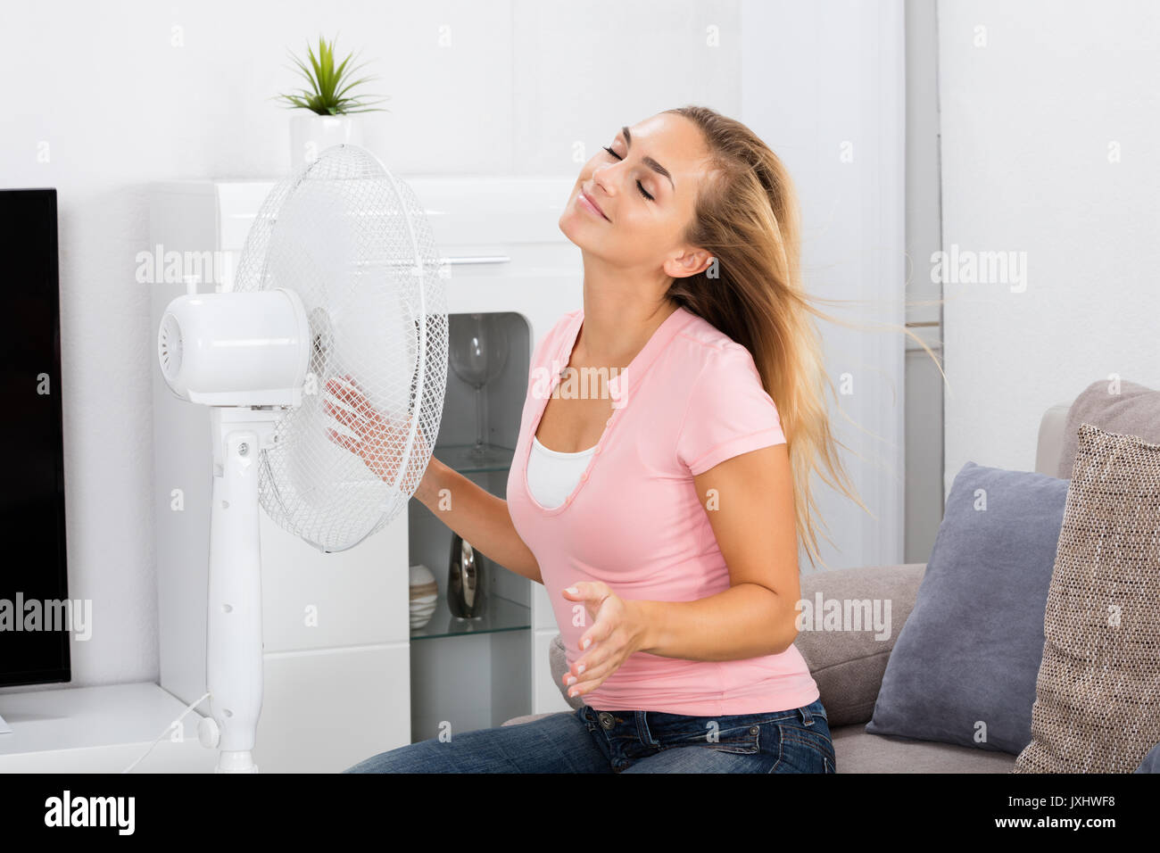 Young Smiling Woman Sitting On Couch In Front Of Fan During Hot Weather ...