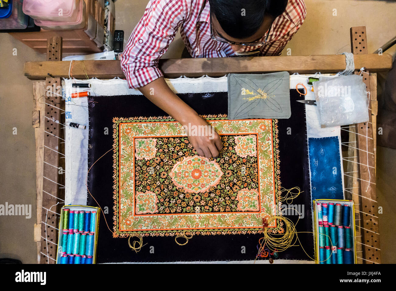 A man creating an embroidered Zardozi wall hanging viewed from above ...