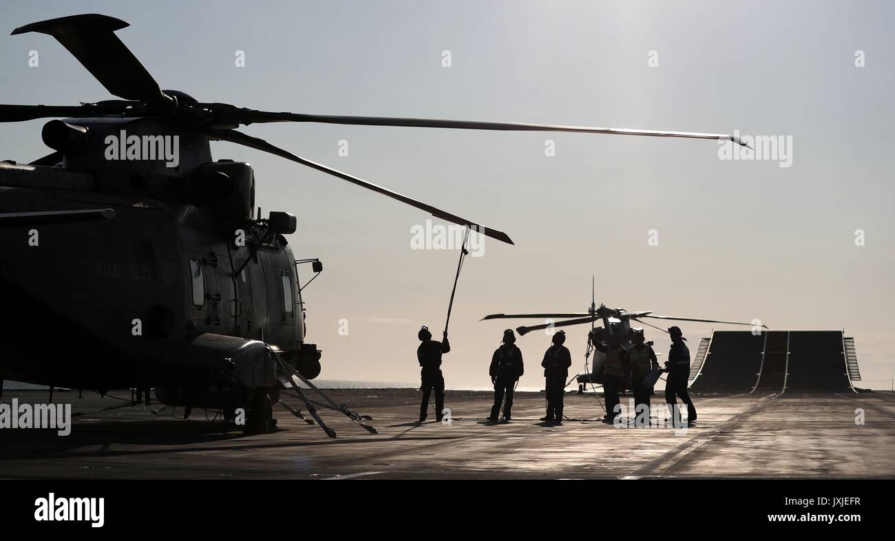 Crew members secure the blades of a Merlin helicopter on the flight ...