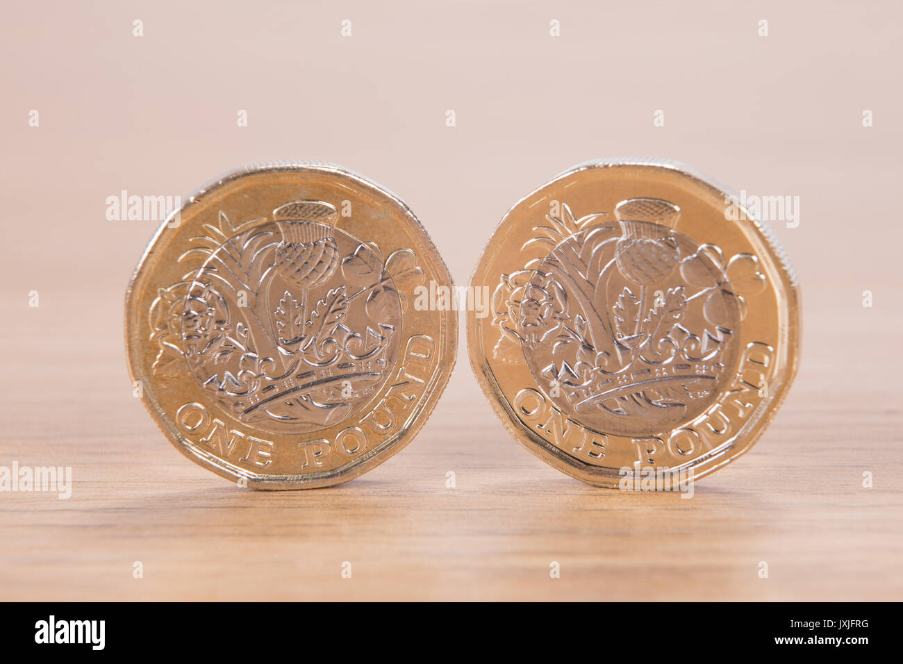 Two pound coins balancing on edge on a wooden table showing the ...