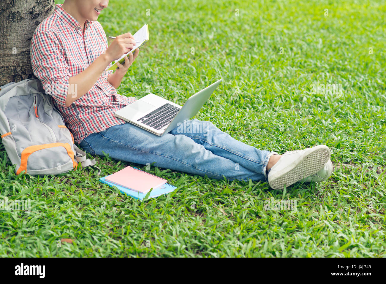 Asian student writing compositions in copybooks sitting on park lawn ...