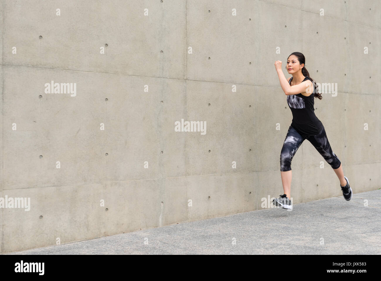 side view photo of smiling female runner running on gray wall ...