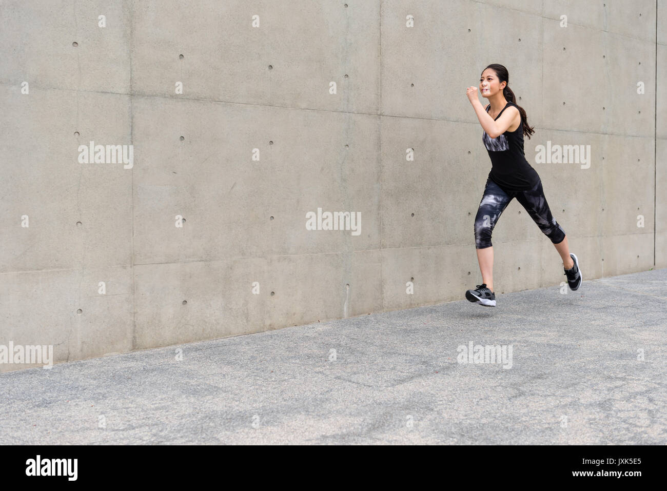 elegant young female jogger jogging on gray background sidewalk in city ...