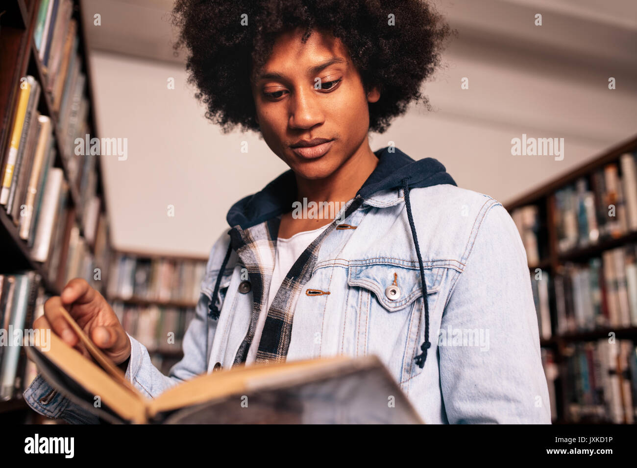 Young african man reading book while standing in a library. college ...