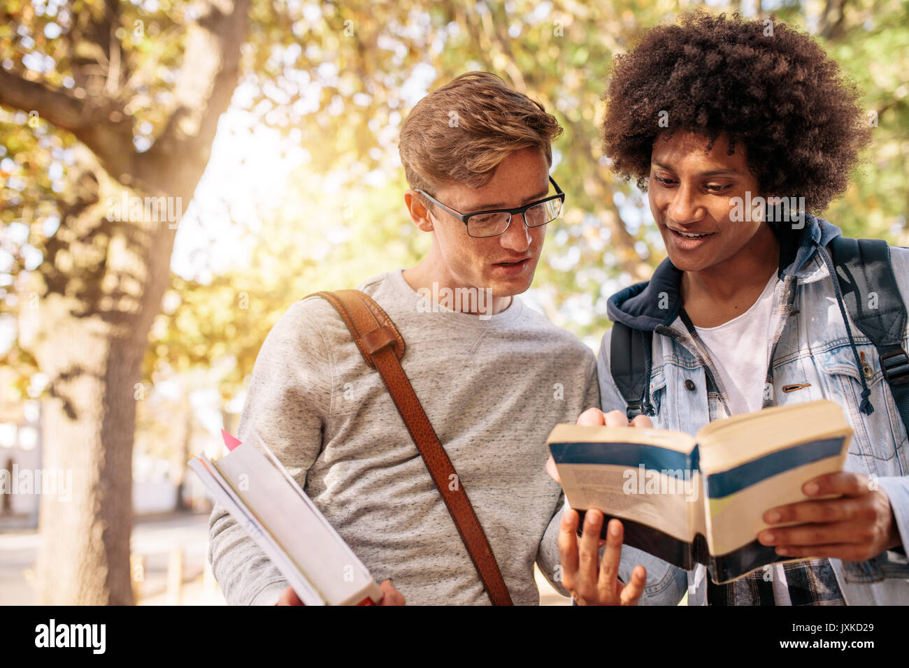 university male students with book on the road. Young students reading ...
