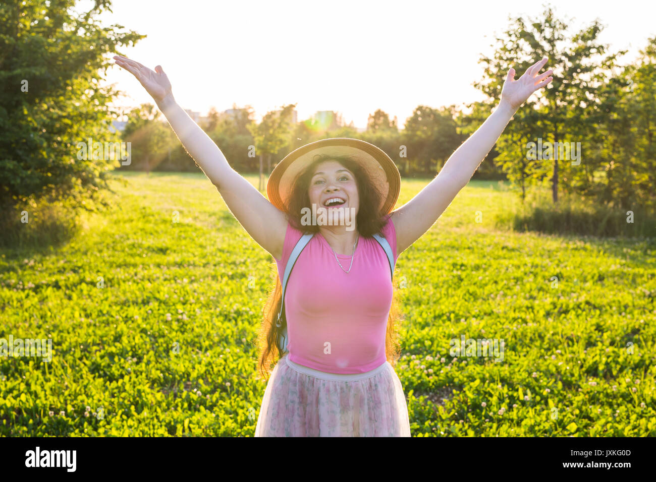 Free happy young woman raising arms watching the sun in the background ...