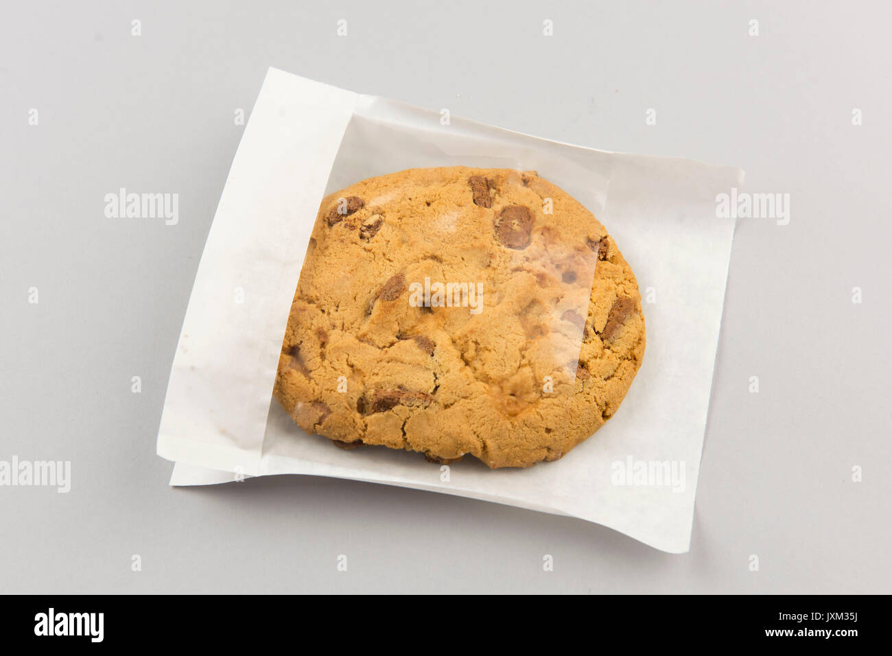 A chocolate chip cookie in a white paper packet on a white background ...