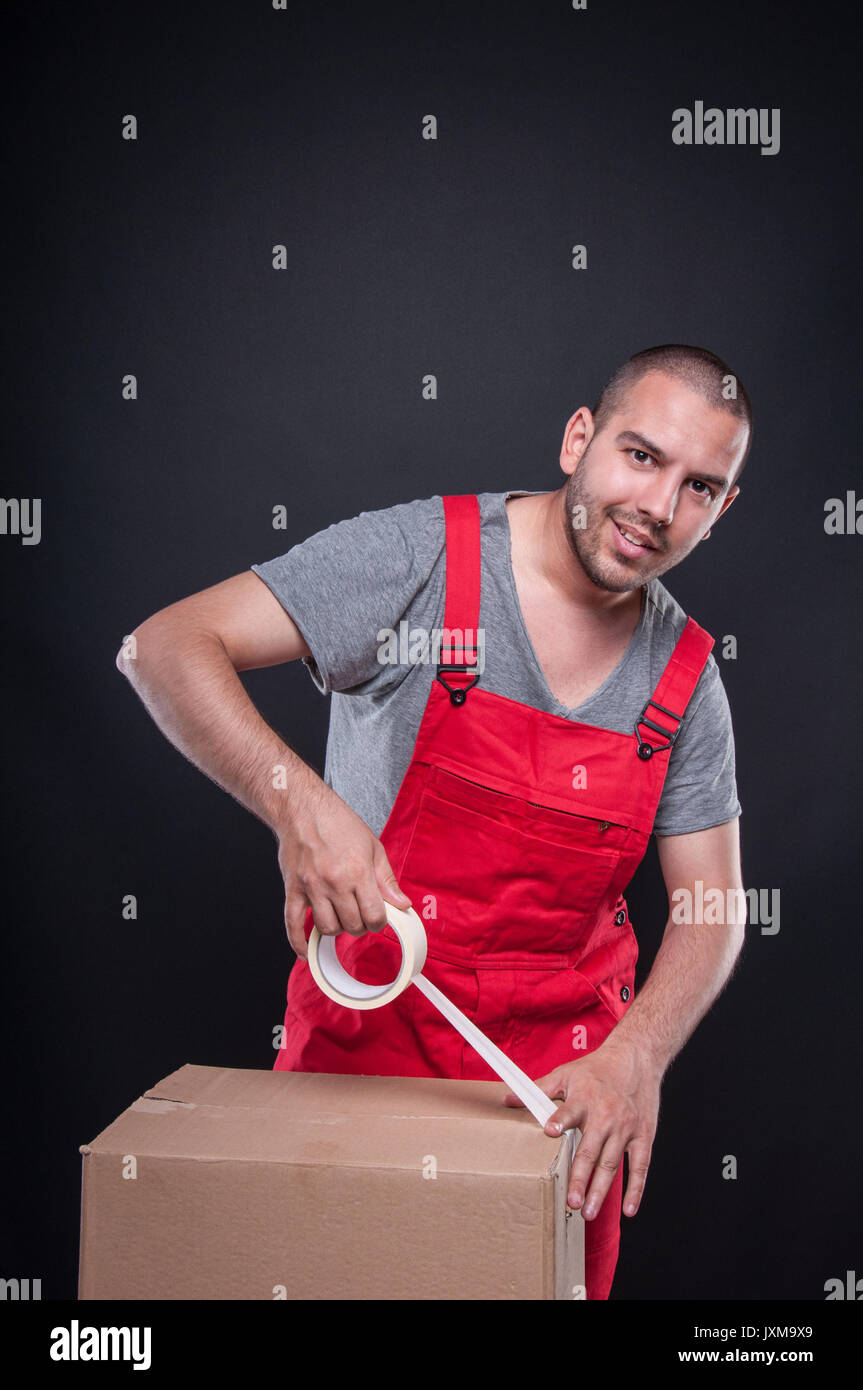 Mover guy packing box with duct tape and smiling on black background ...