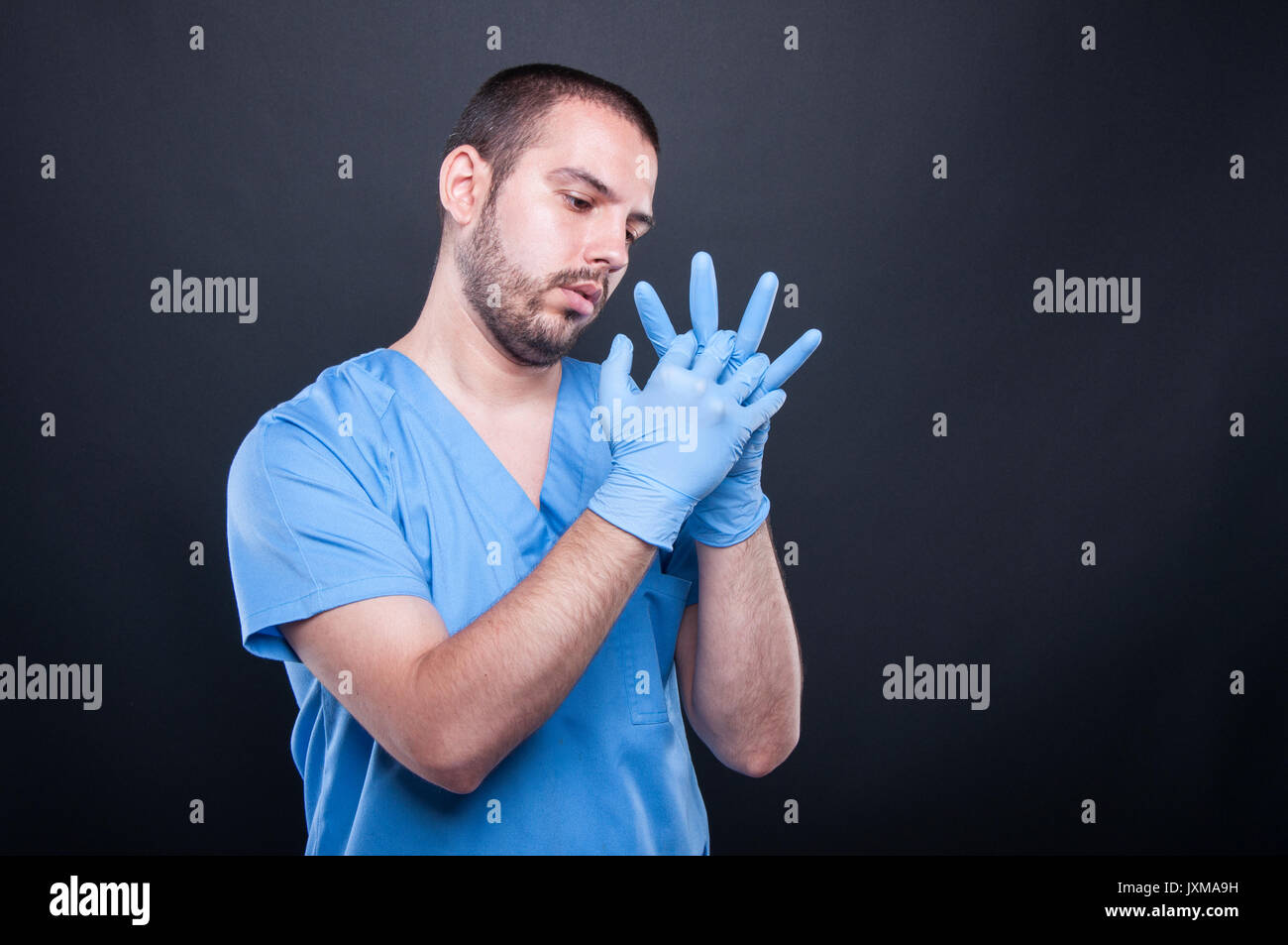 Doctor with scrubs fixing his latex gloves on black background with ...