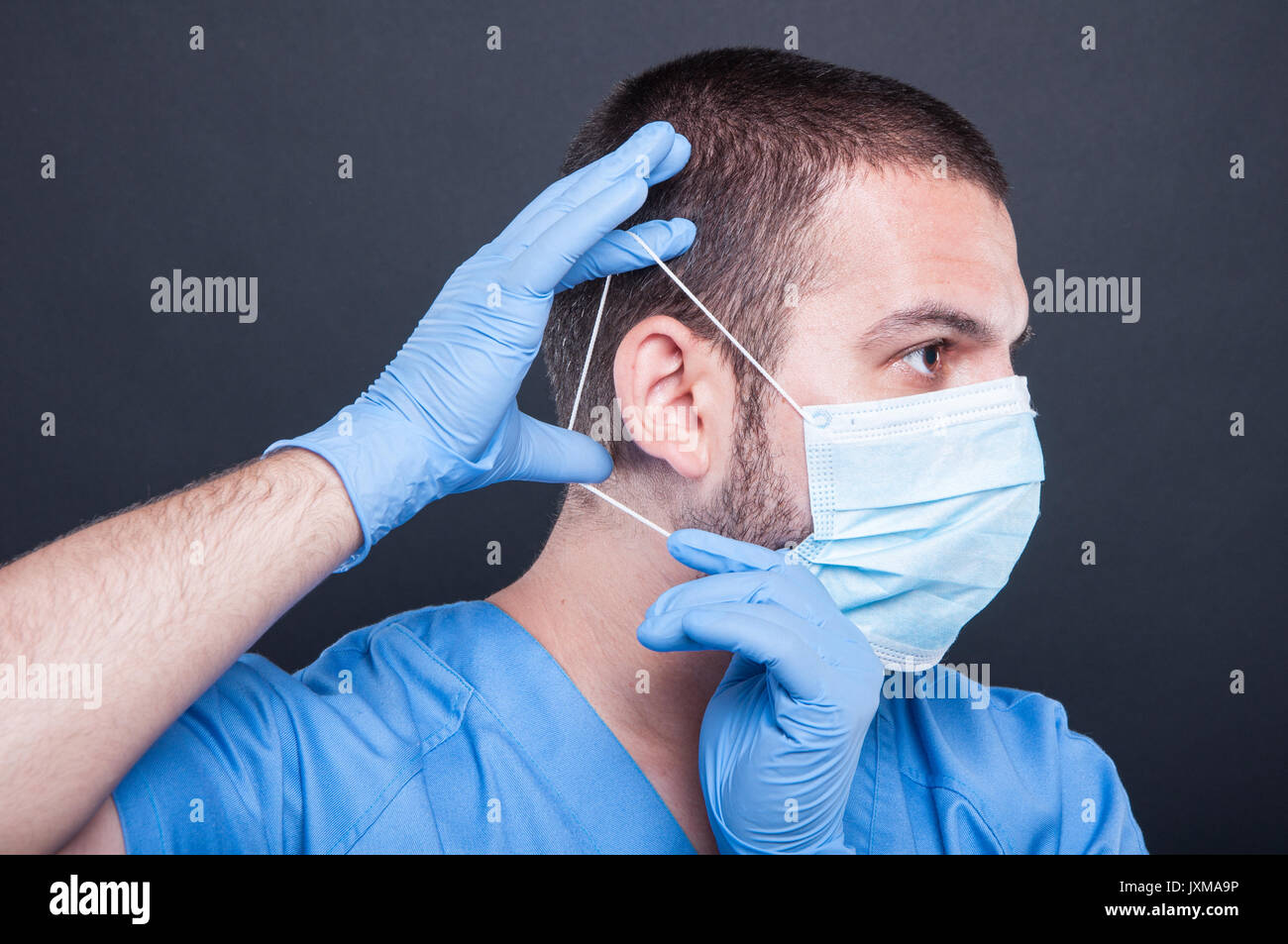 Side view doctor with scrubs and gloves putting on his sterile mask on ...