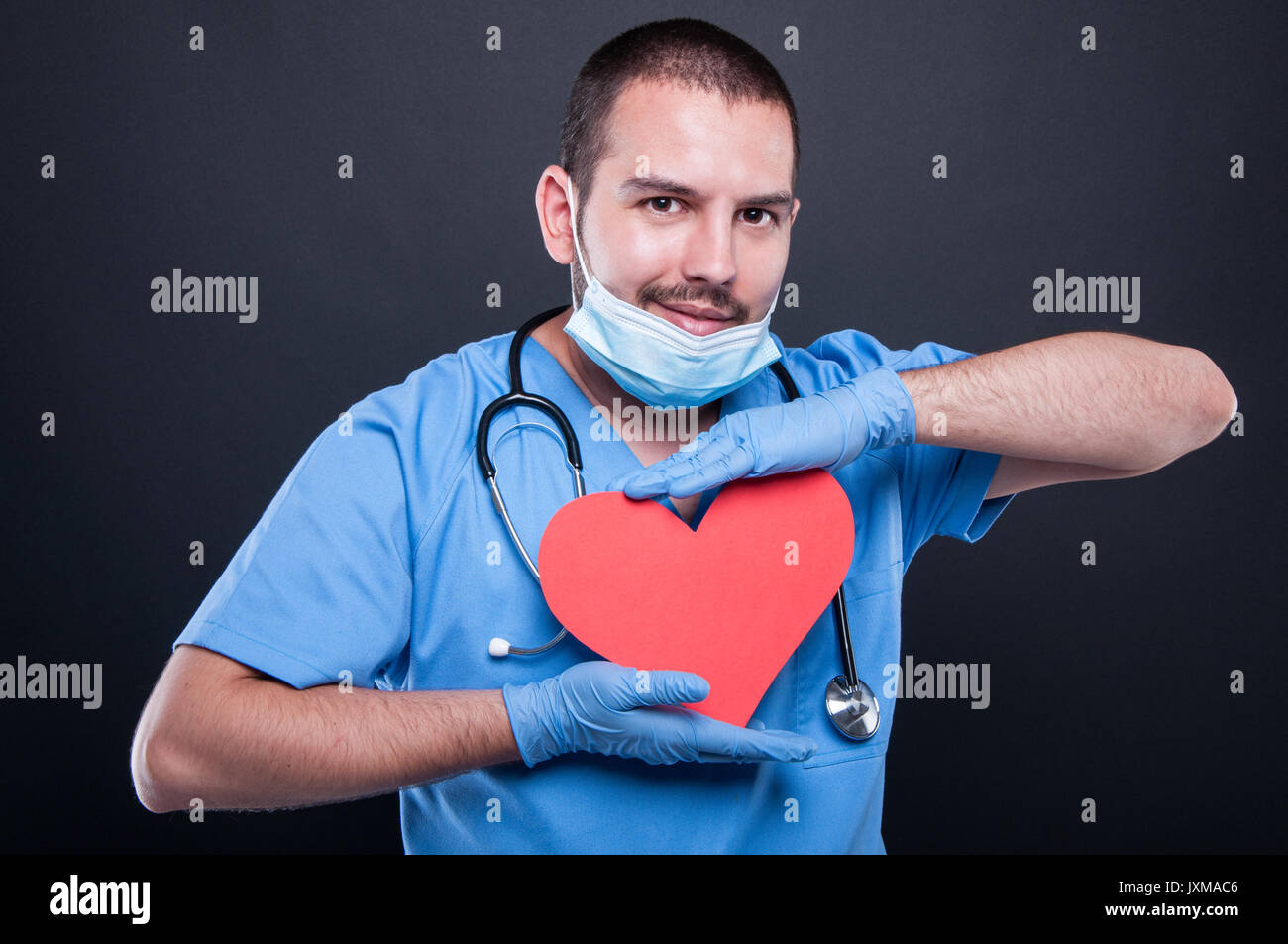 Cardiologist wearing scrubs holding red heart shape on black background ...