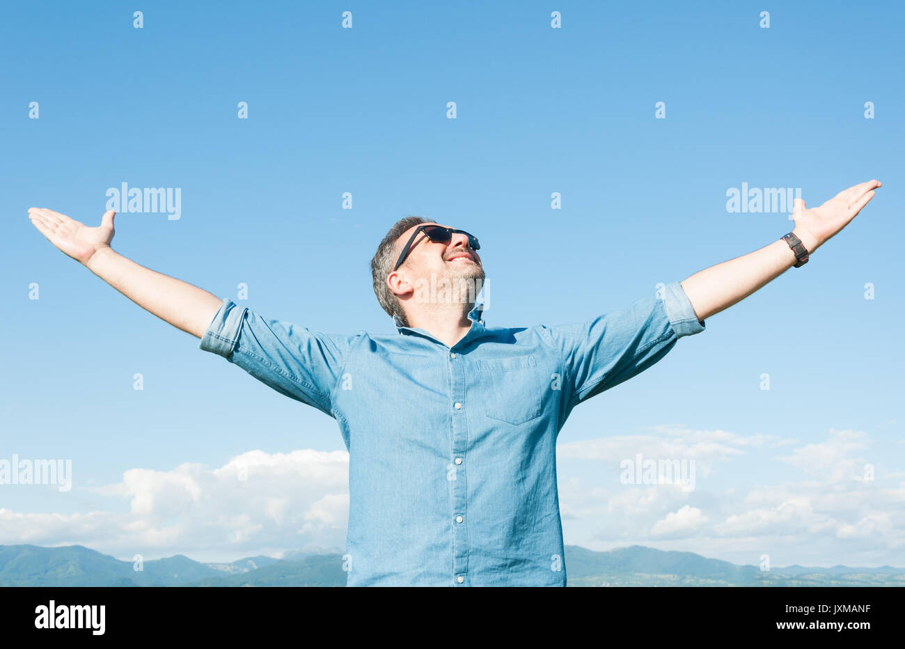 Man feeling good and enjoying nature with raised hands on blue sky ...