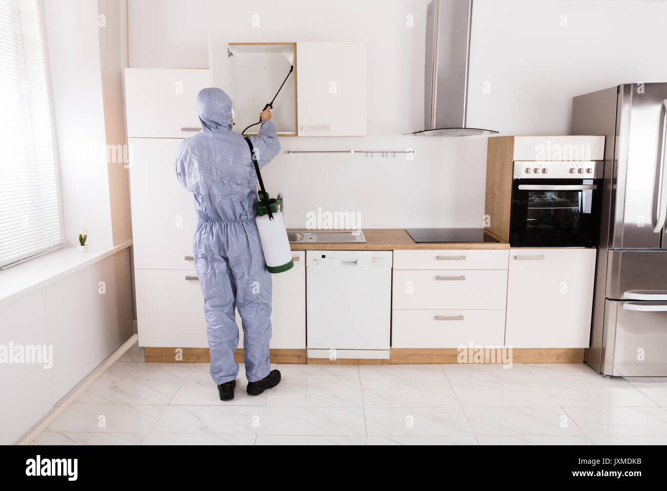 Pest Control Worker In Workwear Spraying Pesticide On Shelf In Kitchen ...
