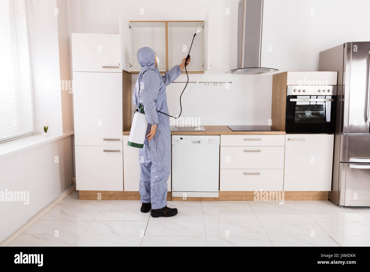 Pest Control Worker In Workwear Spraying Pesticide On Shelf In Kitchen ...