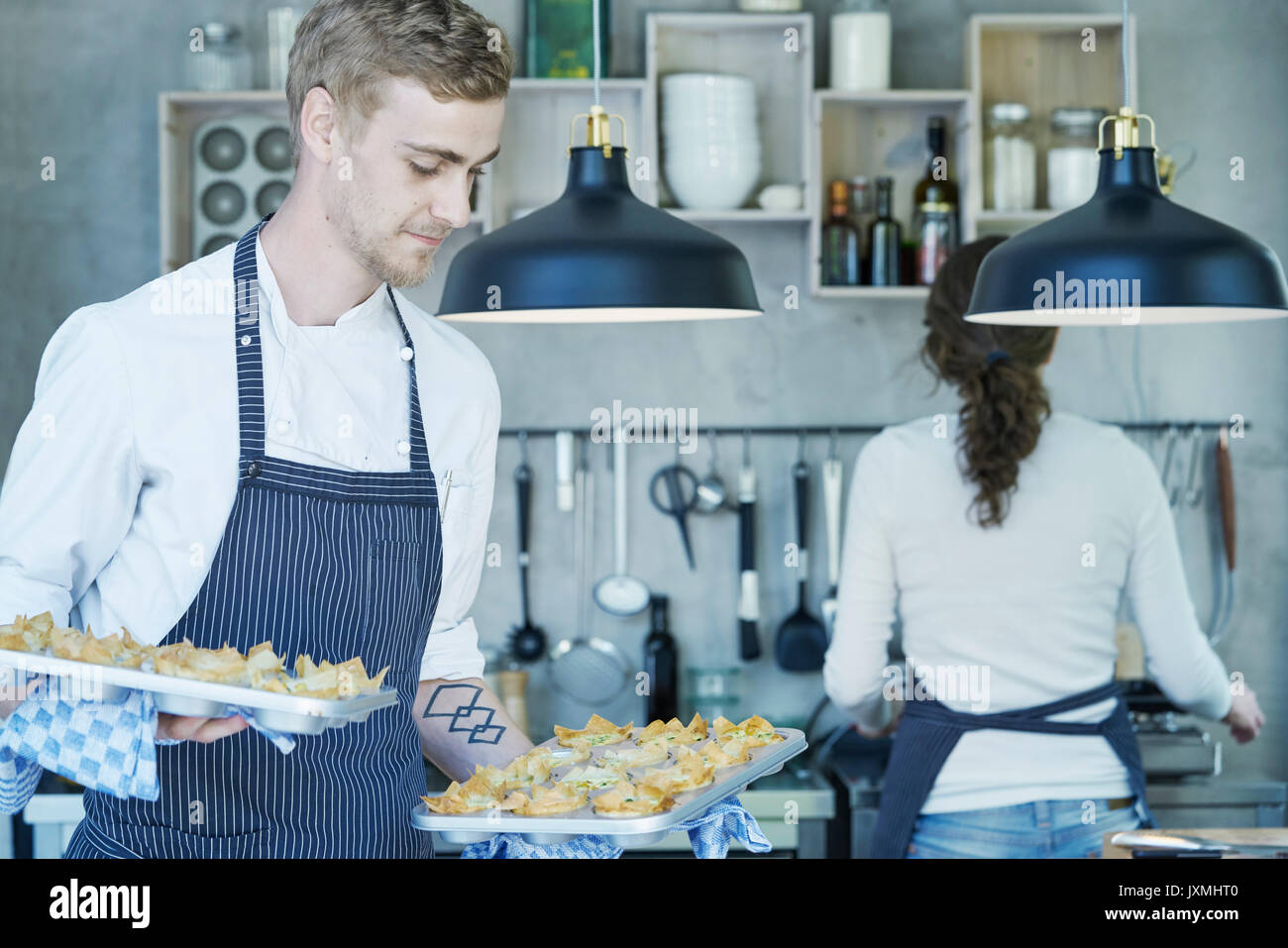 Chef in kitchen, holding baking trays of canapes Stock Photo - Alamy