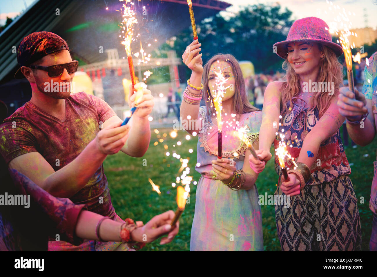 Young adults covered in coloured chalk powder holding sparklers at ...
